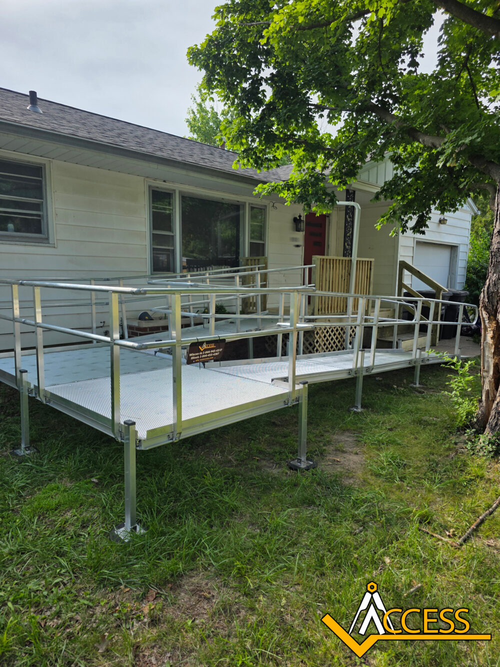 A silver metal wheelchair ramp with railings is installed outside a ...