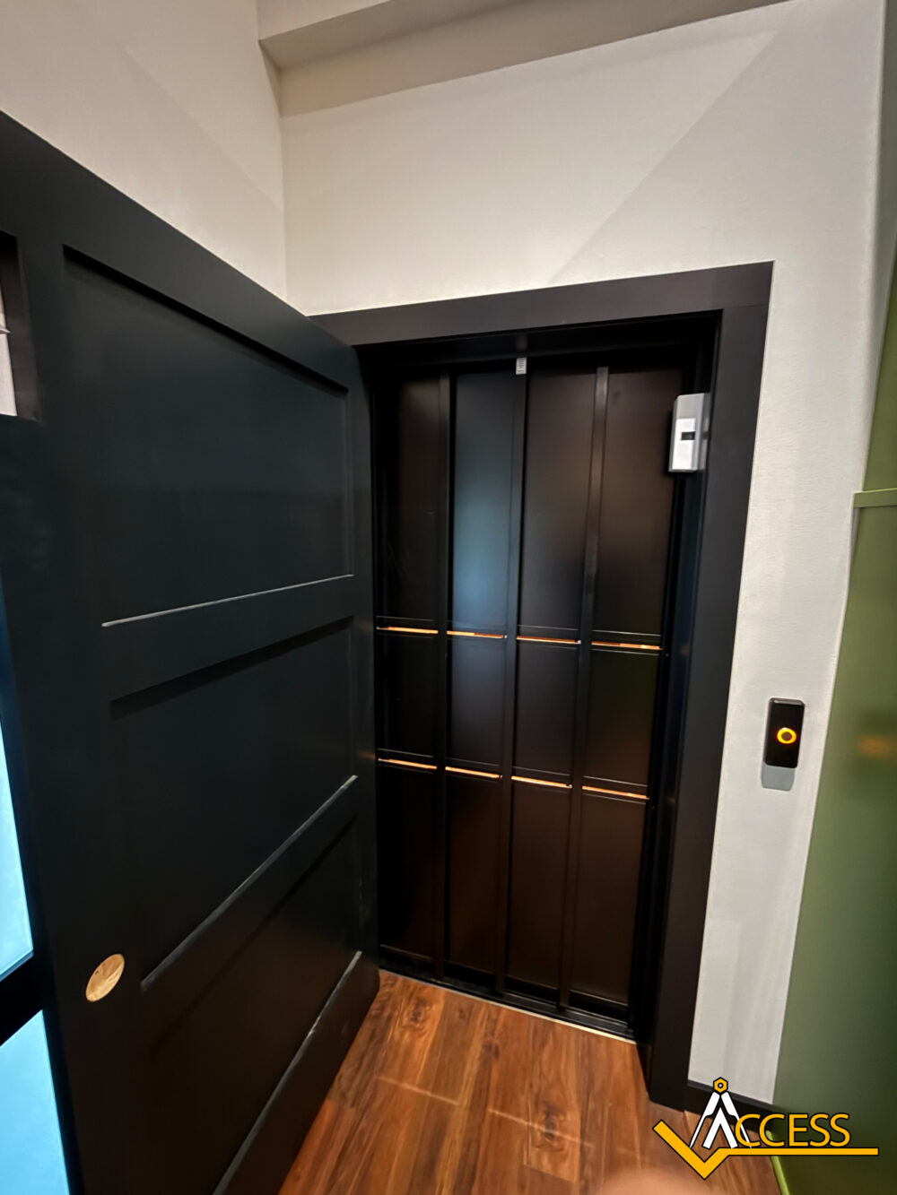 A small, modern residential elevator with black sliding doors and gold ...