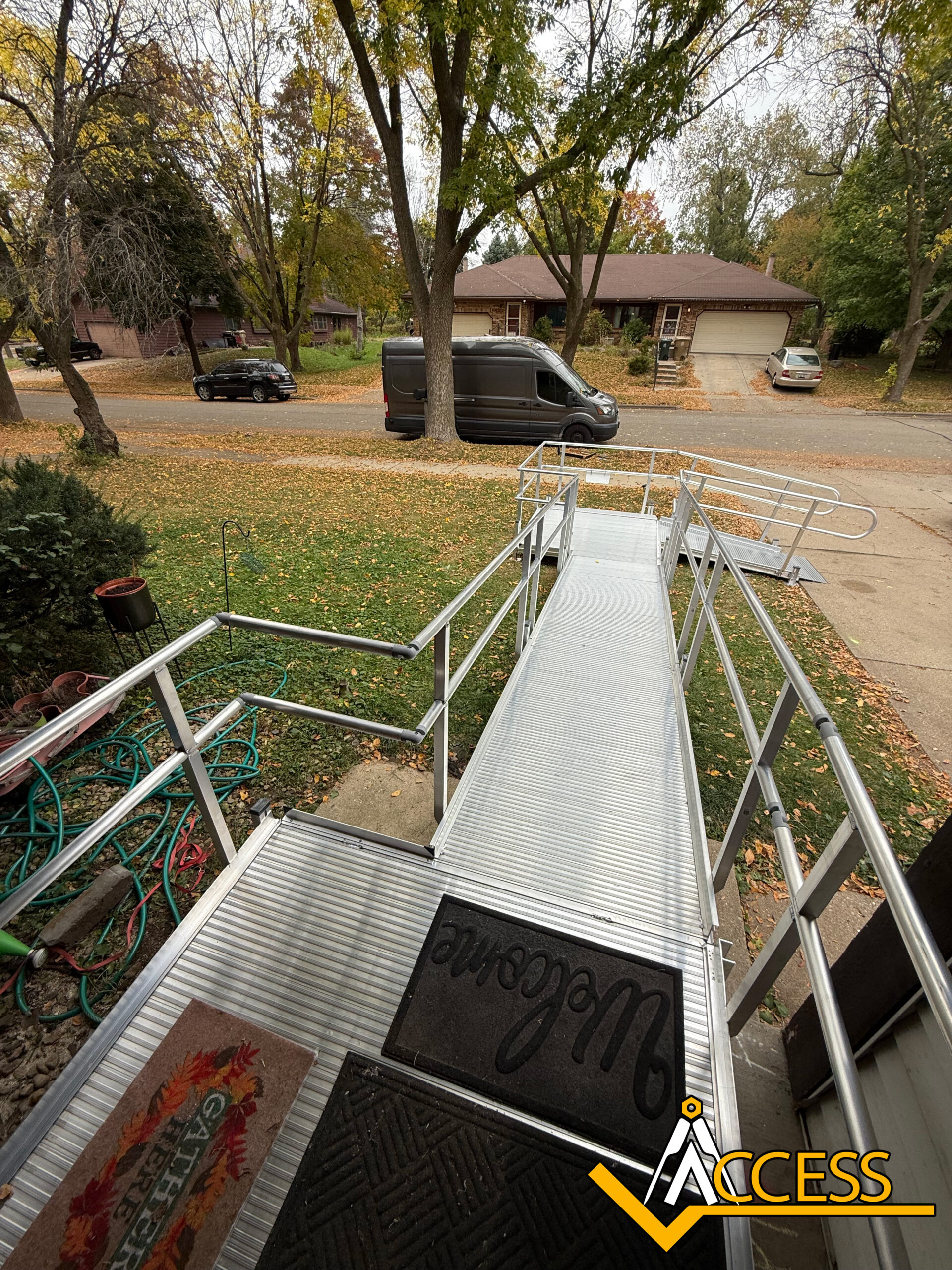 A metal wheelchair ramp leads from a house to the sidewalk, surrounded ...