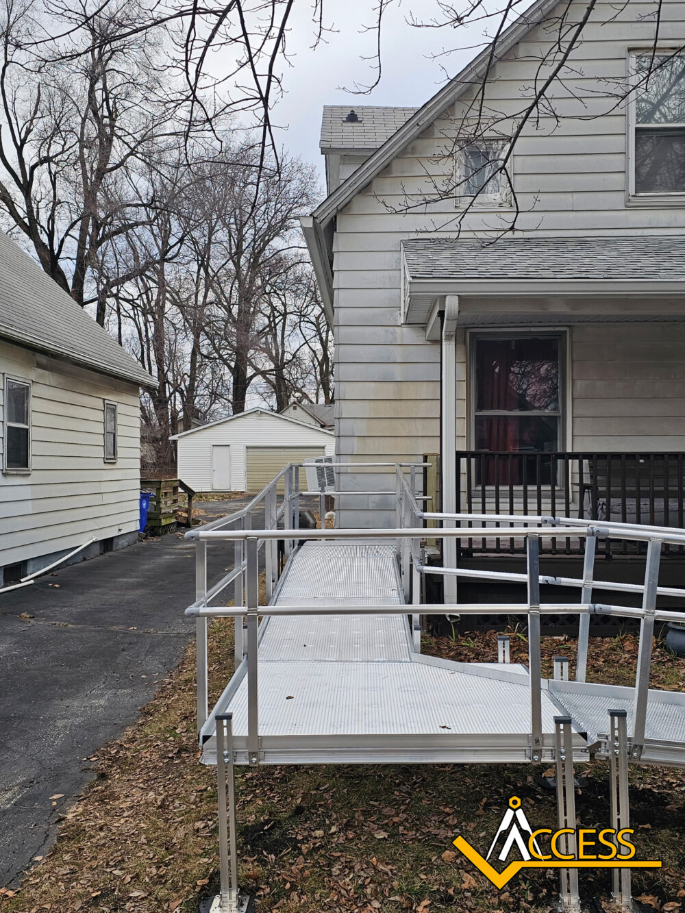 A metal wheelchair ramp leads from a driveway to the porch of a gray ...
