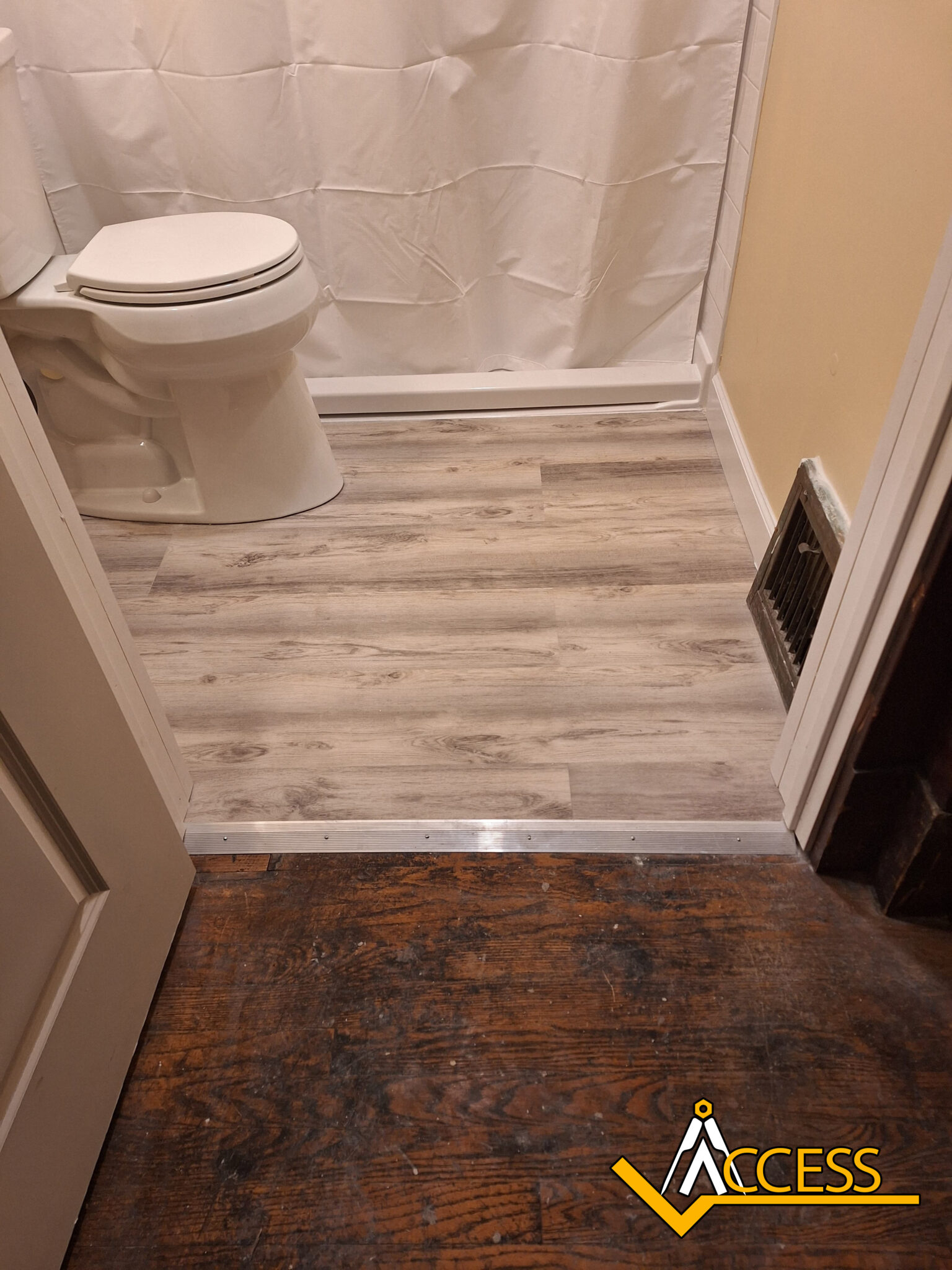 A bathroom with light wood-look vinyl flooring, a white toilet, cream ...