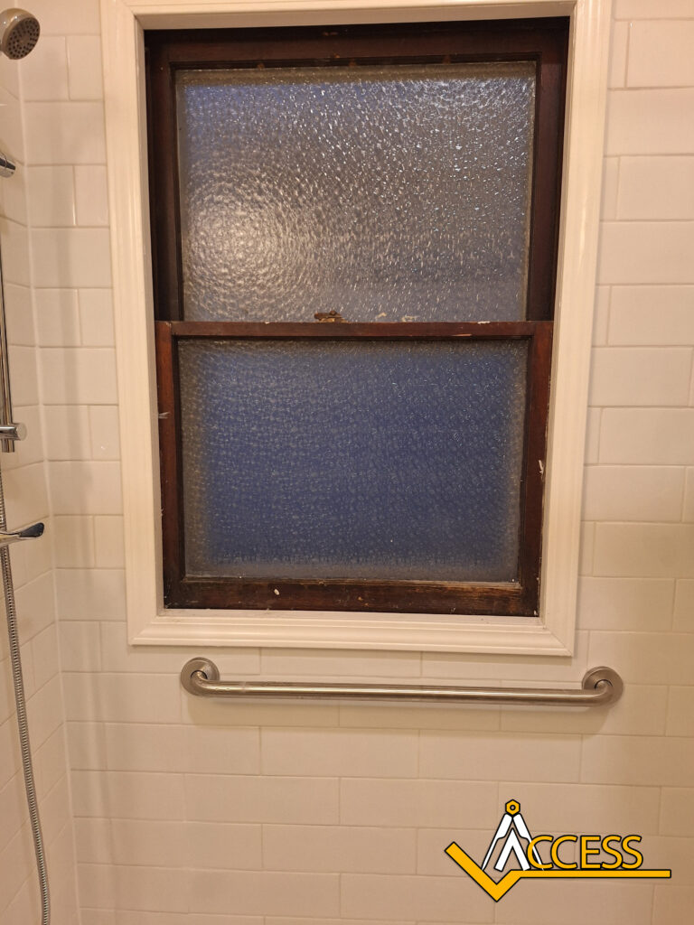A bathroom window with frosted glass and a dark wooden frame is set in ...